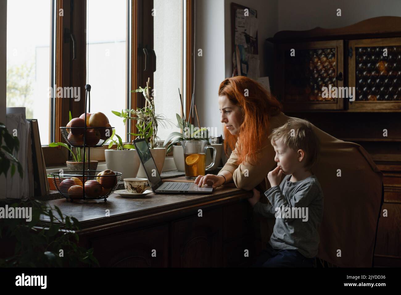 Ginger haired woman on kitchen with child looking in laptop. Vintage ...