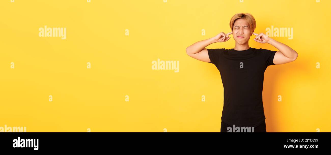 Portrait of annoyed and bothered asian guy grimacing, shut ears ...