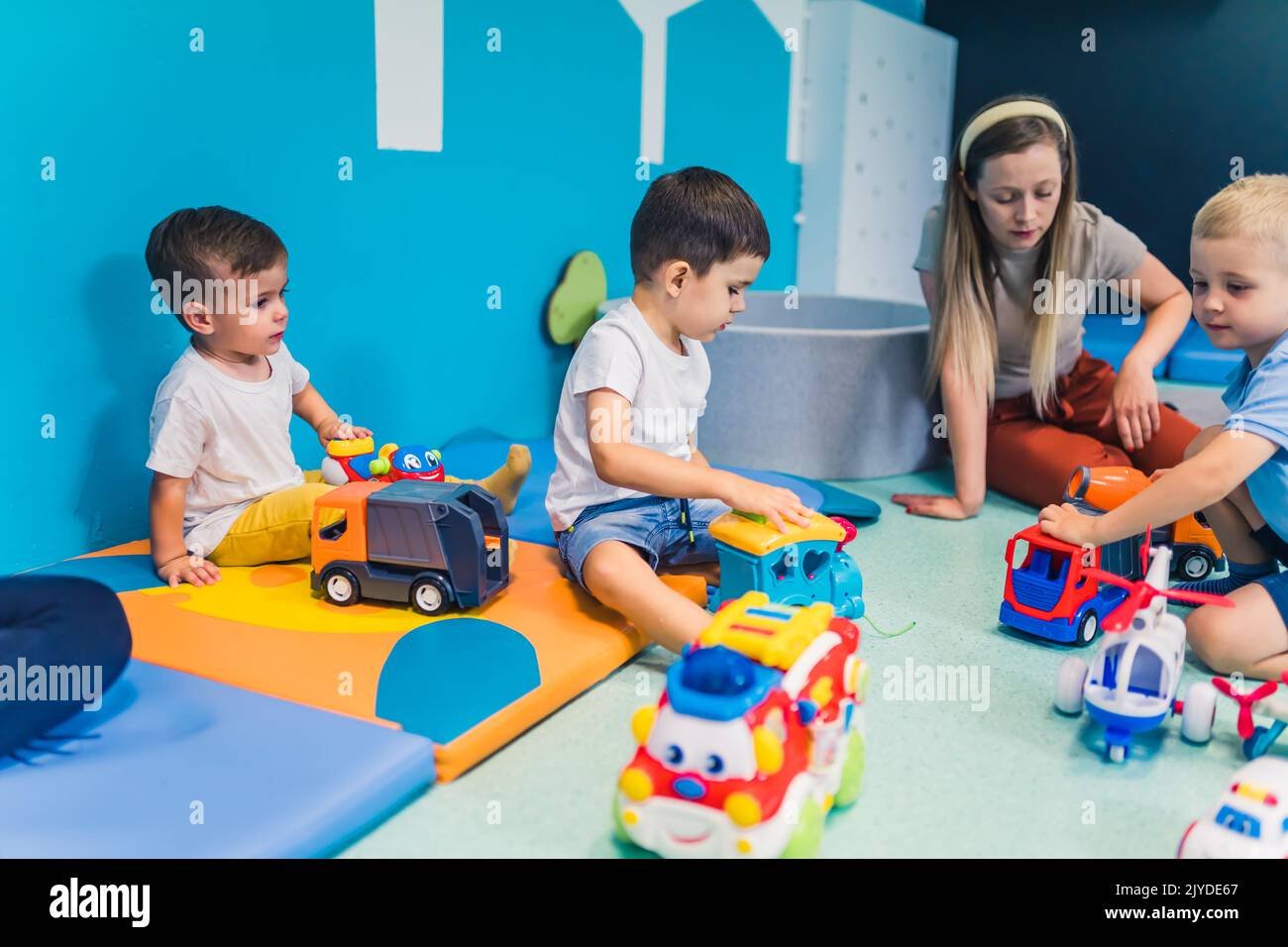 Toddlers and their nursery teacher playing with plastic building blocks ...