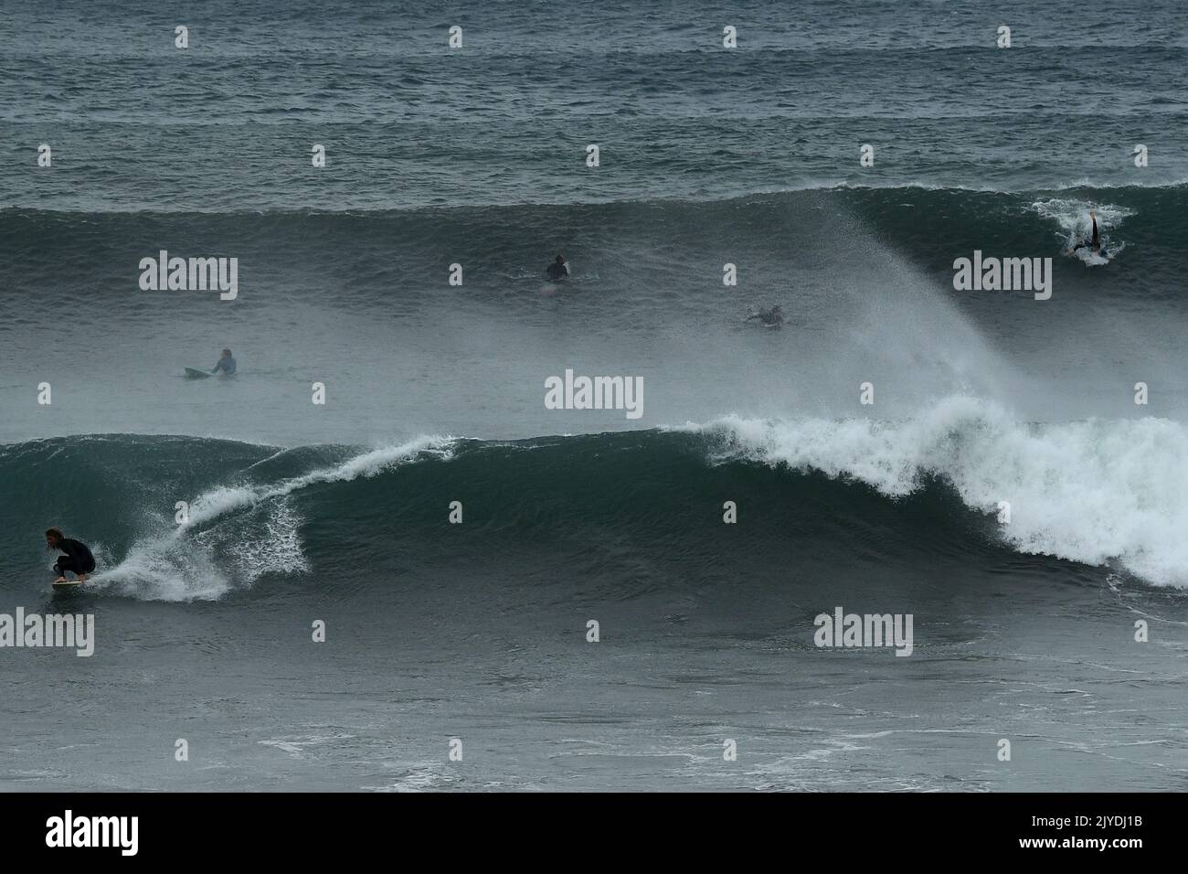 A surfer is seen riding a wave during big swells at Collaroy Beach in ...
