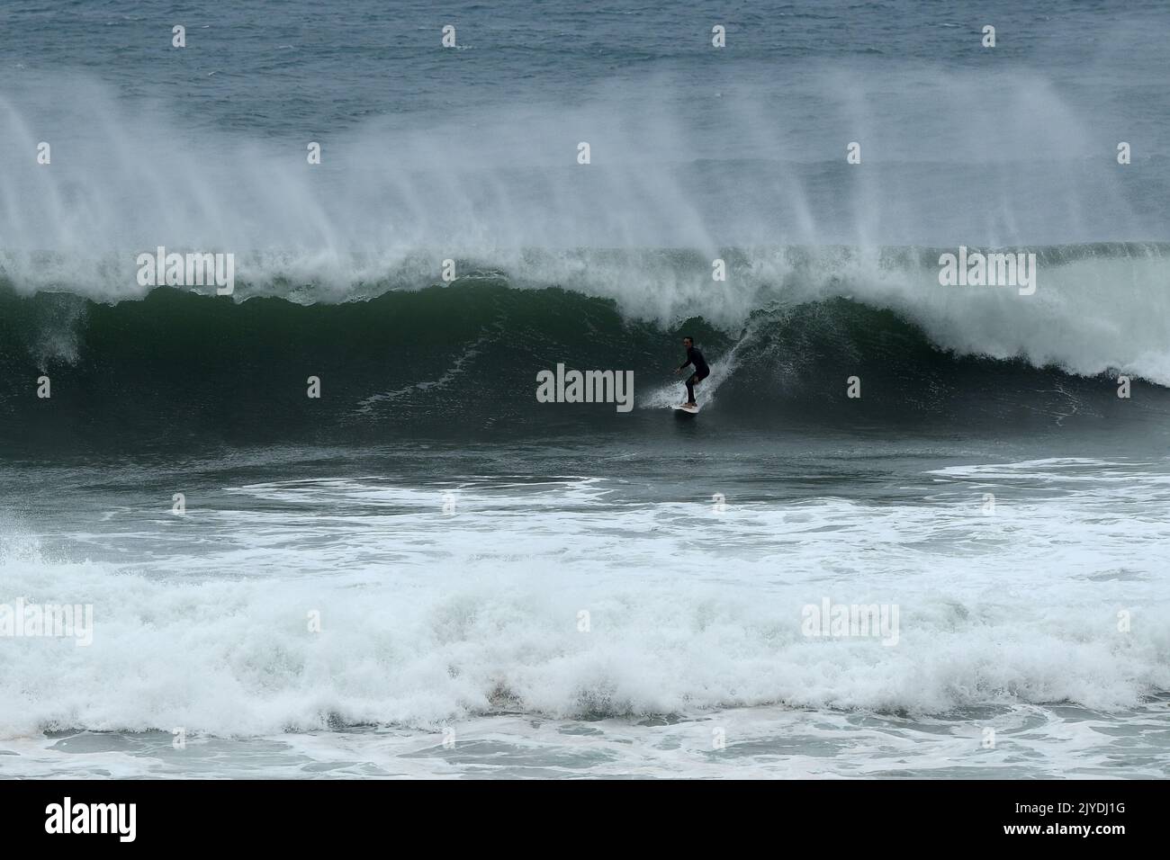 A surfer is seen riding a wave during big swells at Collaroy Beach in ...