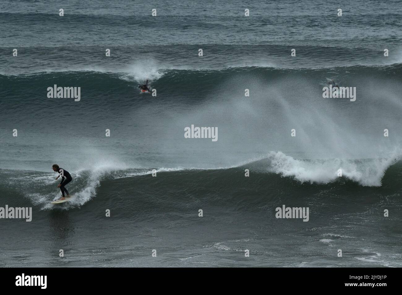 A surfer is seen riding a wave during big swells at Collaroy Beach in ...