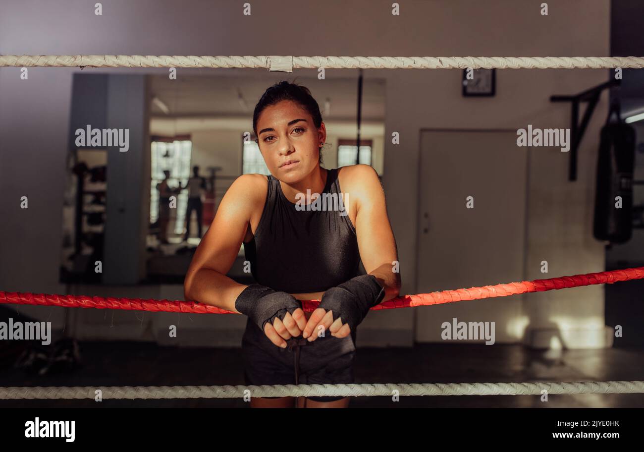 Confident female boxer looking at the camera while leaning on the ropes ...