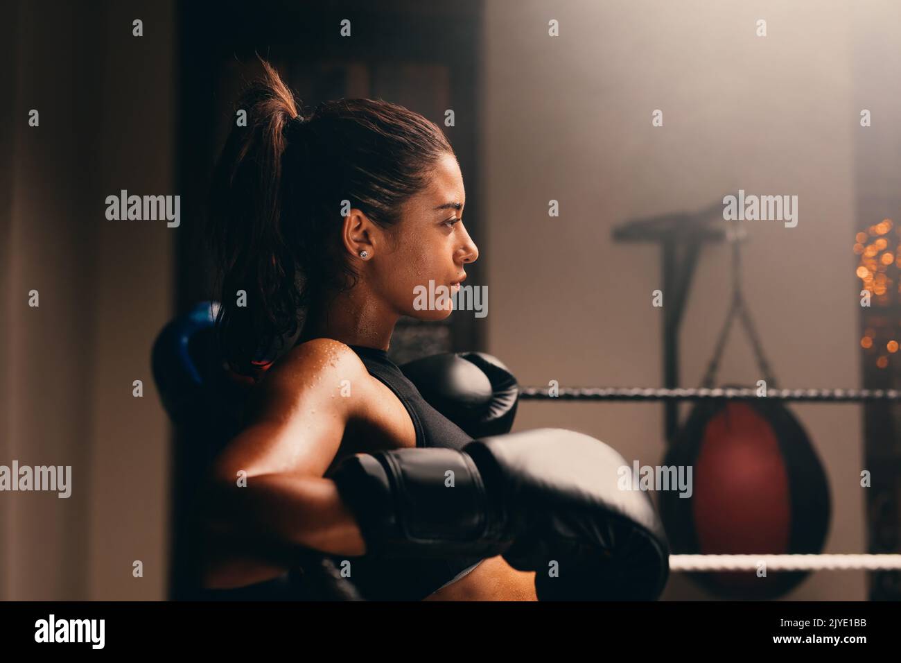 Sideview of a young female boxer leaning against the ropes in boxing ...