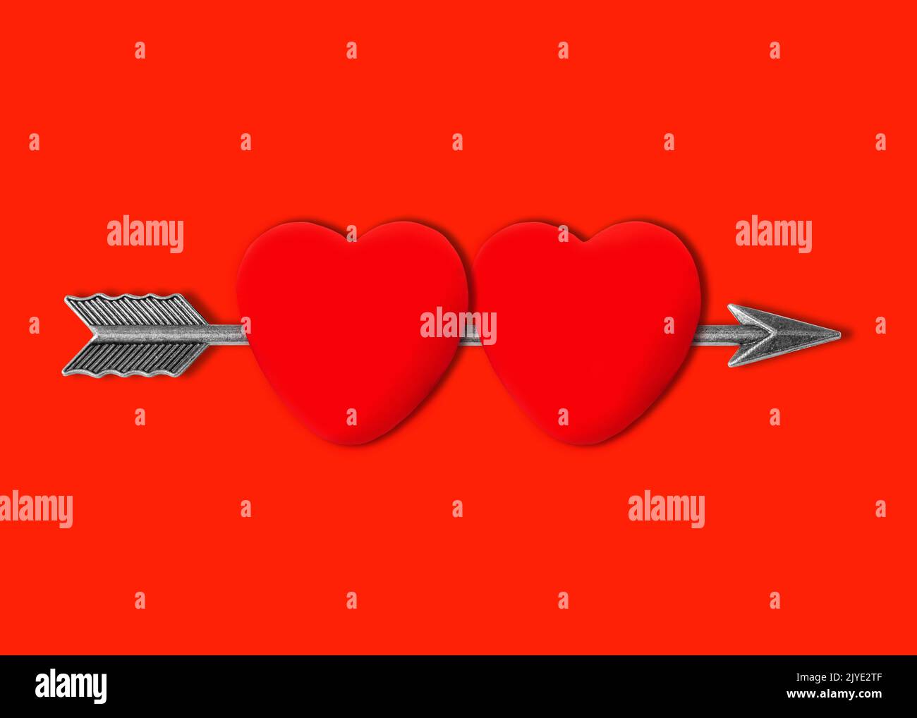 Feathered bow arrow passing through two heart shapes isolated on red ...