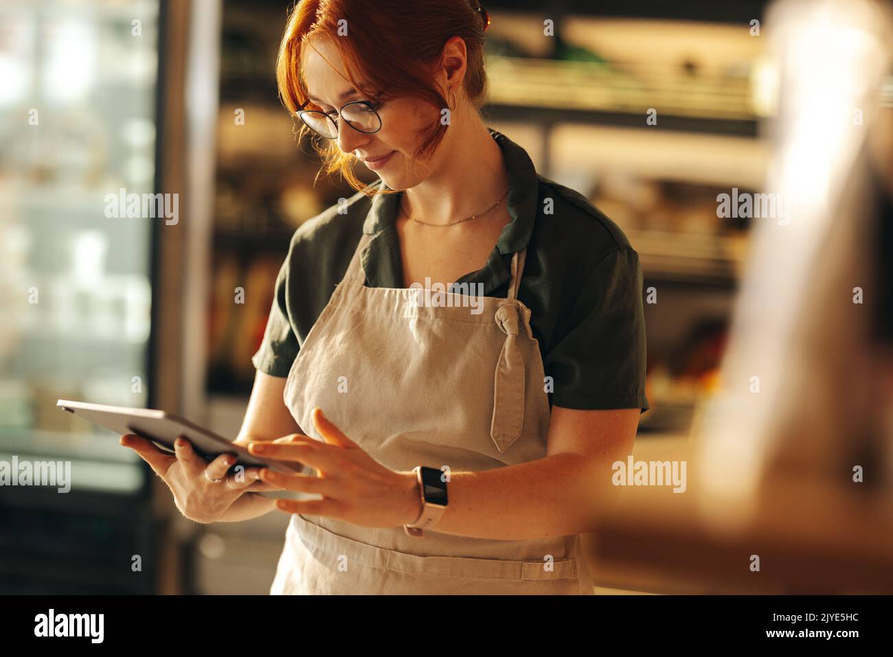 Cheerful supermarket owner using a digital tablet while standing in her ...