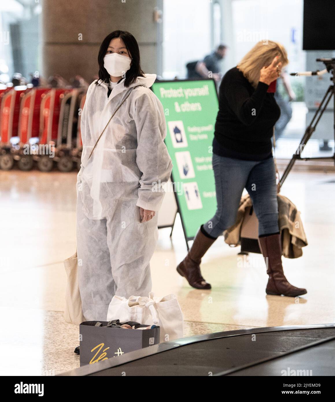 A passenger wearing a protective suit and mask collecting baggage after ...