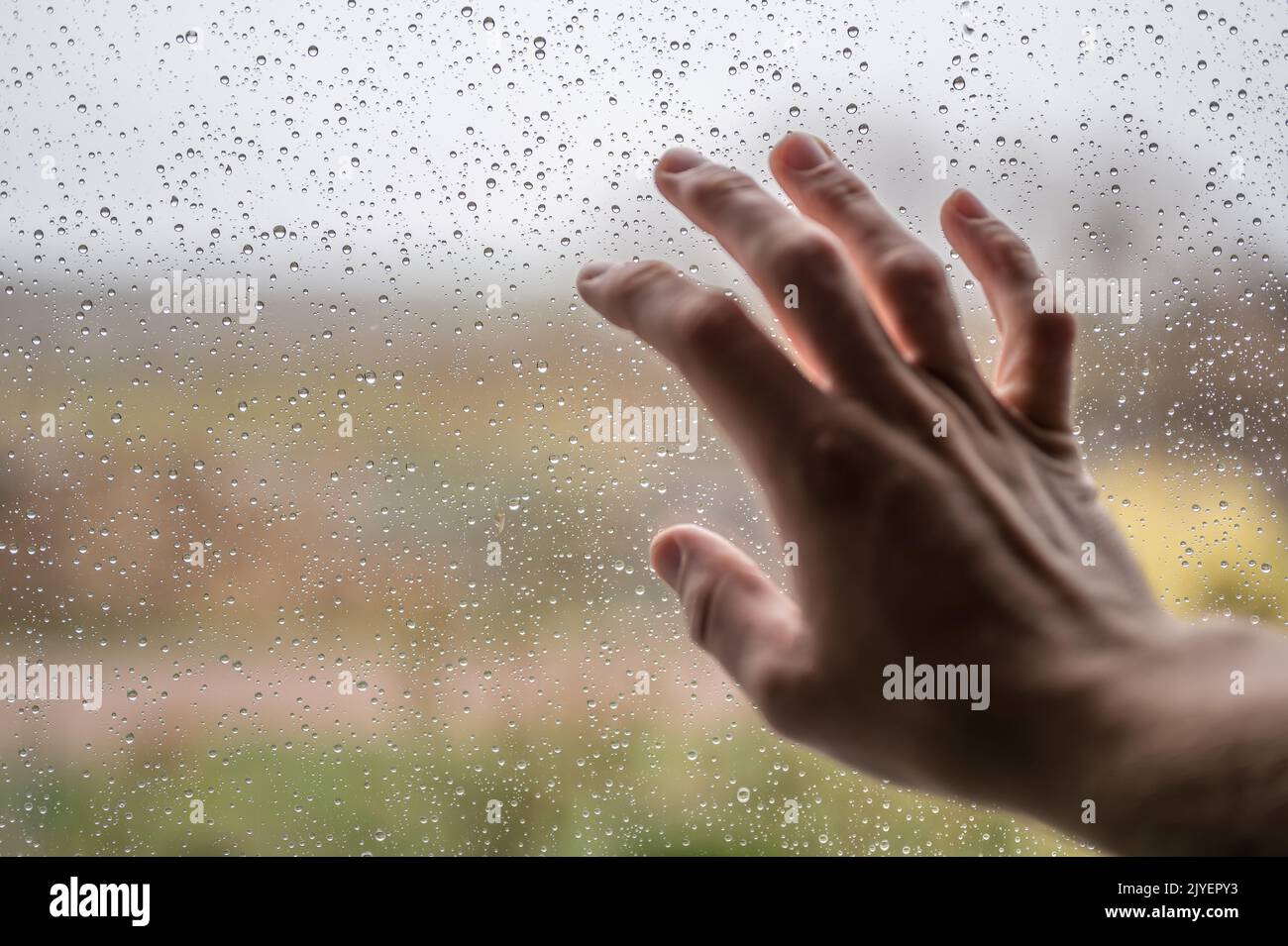 Man touches rain-soaked window pane as a symbol of wanderlust and ...