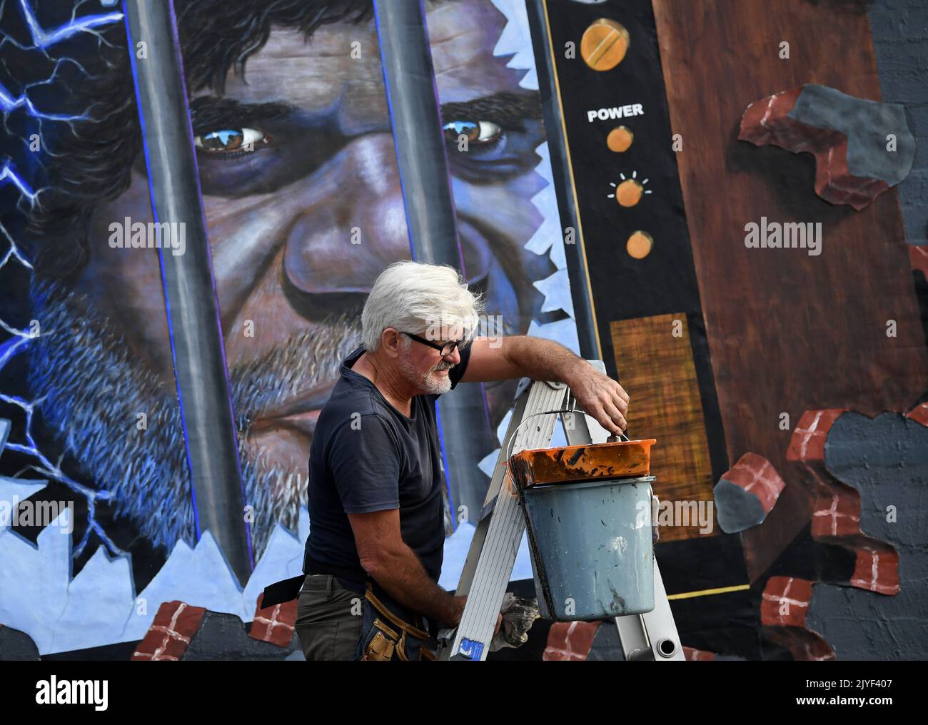 Artist Tim Guider works on a mural titled 'The subtle violence of ...