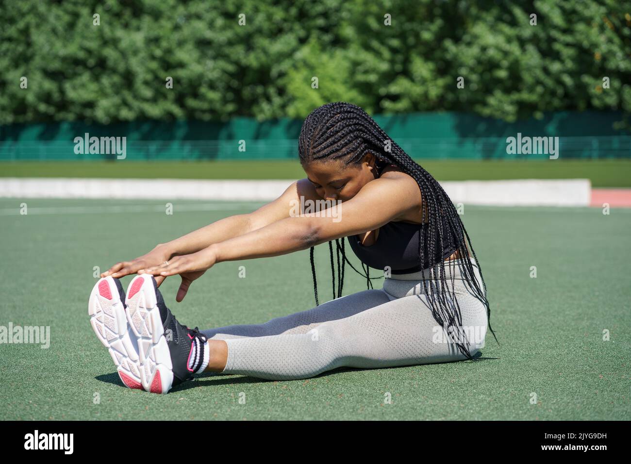 African American woman enjoys stretching back sitting on green turf ...