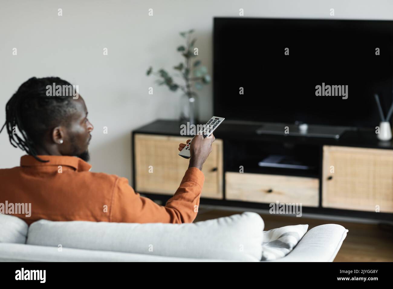 African american man watching television, pointing remote control at ...