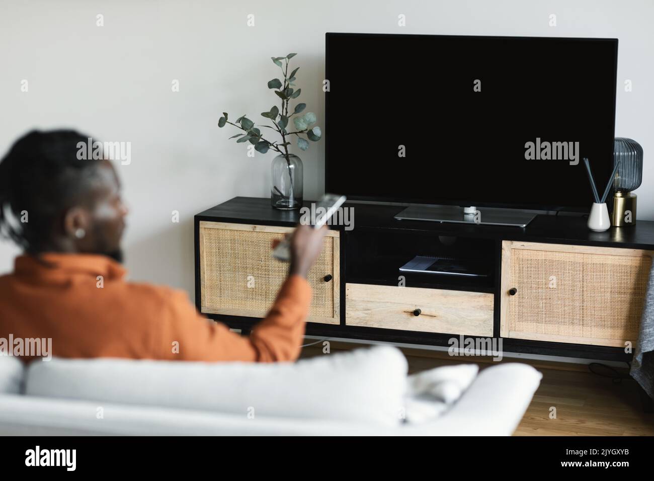Unrecognizable black man turning on plasma flatscreen TV-set, pointing ...