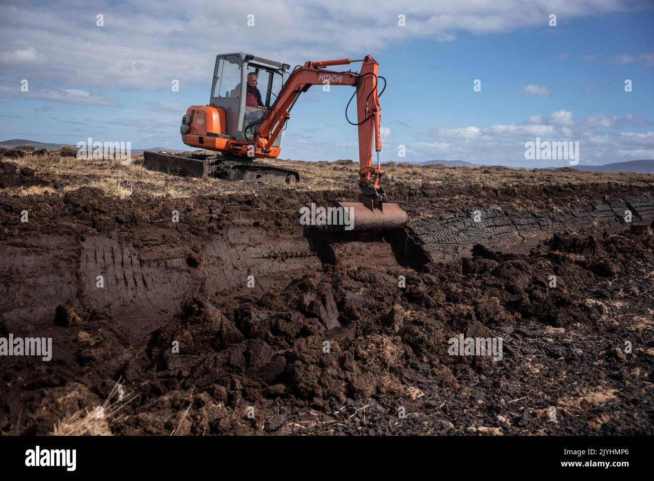 A digger with a bucket on the bog. It digs sods of peat out of the ...