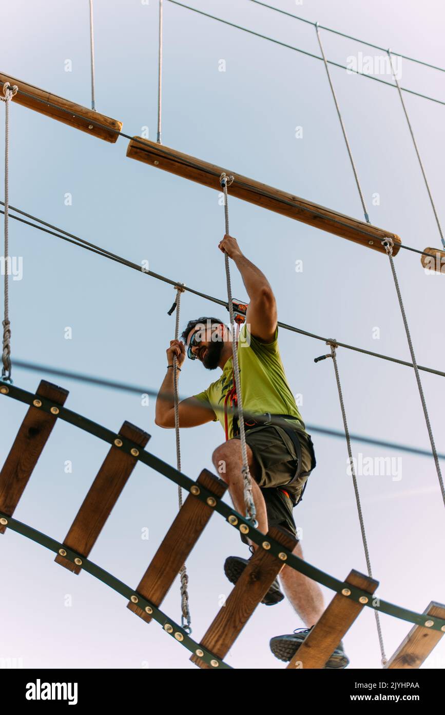 Handsome man balancing himself on the ladder in the adventure park ...