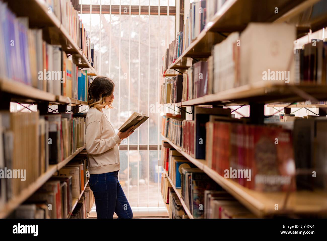 Cute girl reading a book while standing between the bookshelves Stock ...