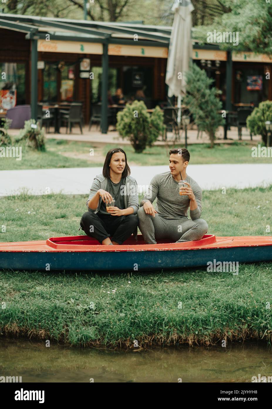 Pretty couple talking while sitting on a kayak in the park drinking ...