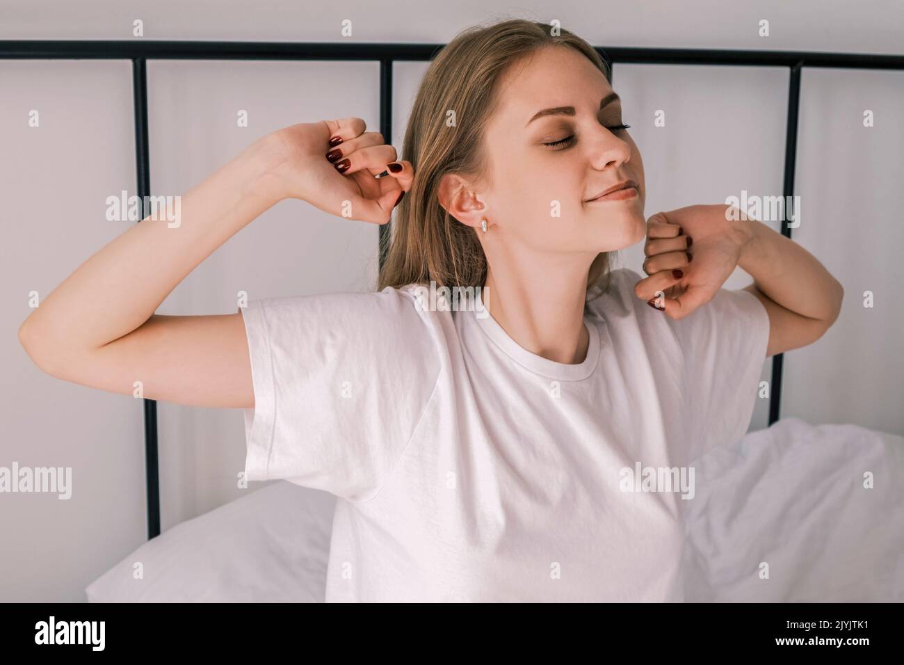 Waking up in the morning. Young sleepy woman stretches out in bed with ...