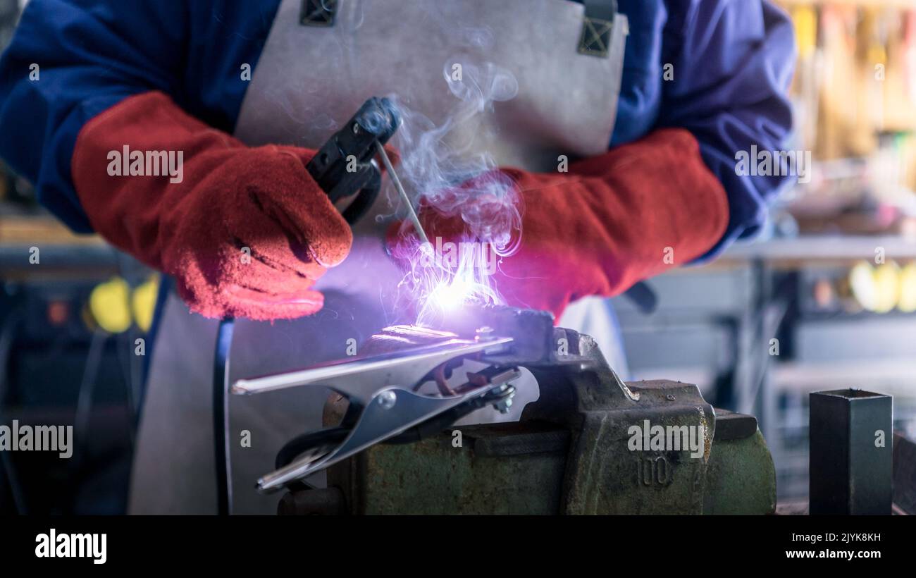Skillful metal worker working with arc welding machine in factory while ...