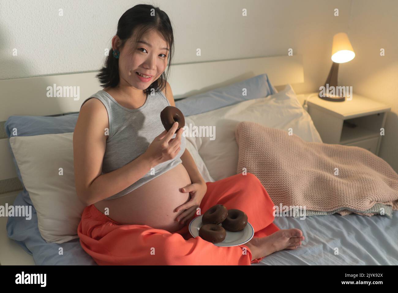 young happy and beautiful Asian Chinese woman pregnant sitting on bed ...