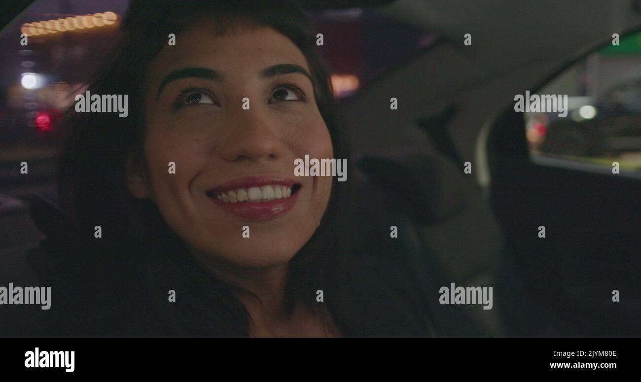 Happy female passenger in backseat of car smiling while looking out taxi window. Young woman ...