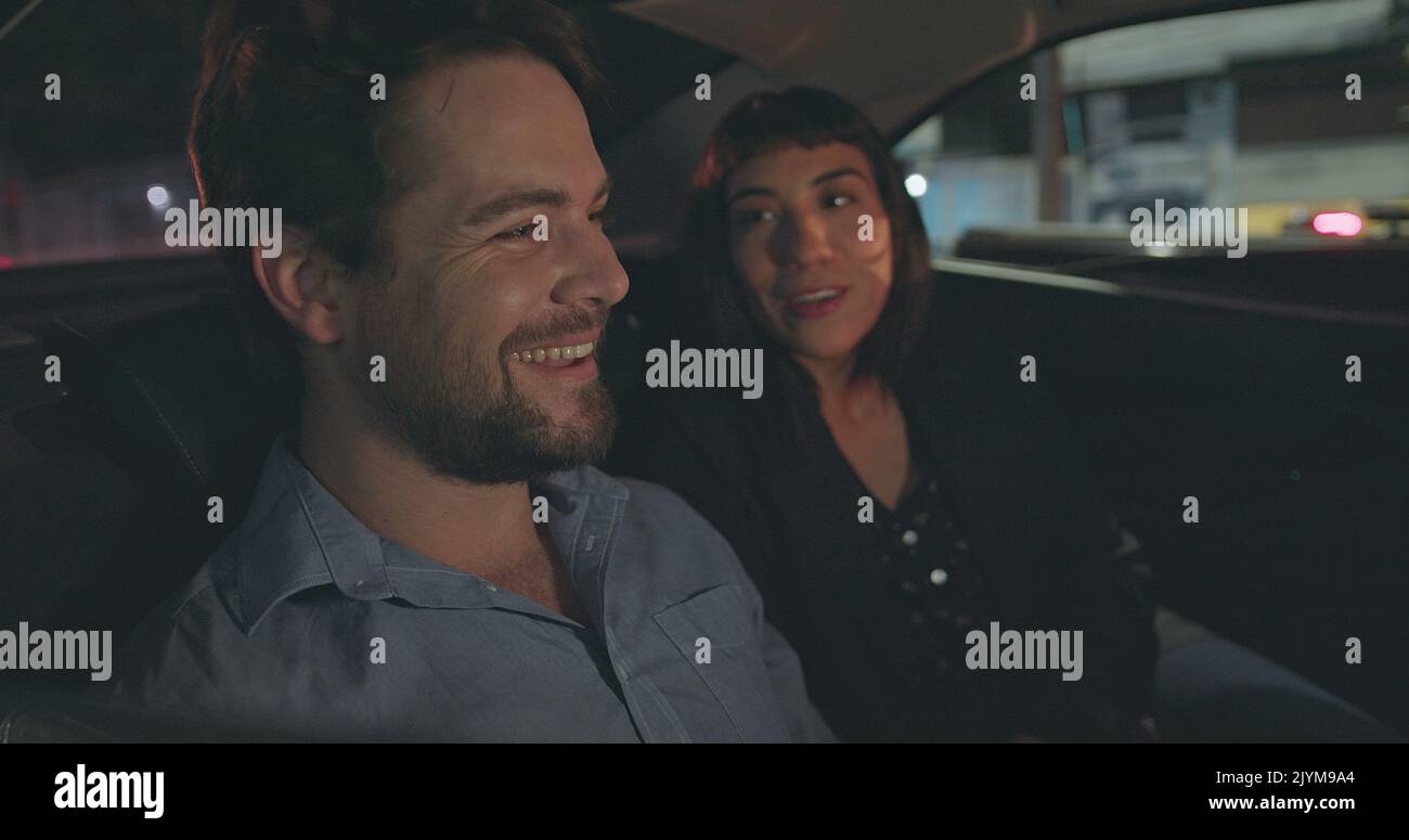 People riding taxi cab looking at car window at night. Man pointing out ...