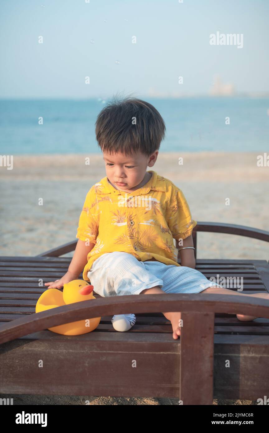 Baby boy on a beach holiday sitting on the sunbed at sunset. One year ...