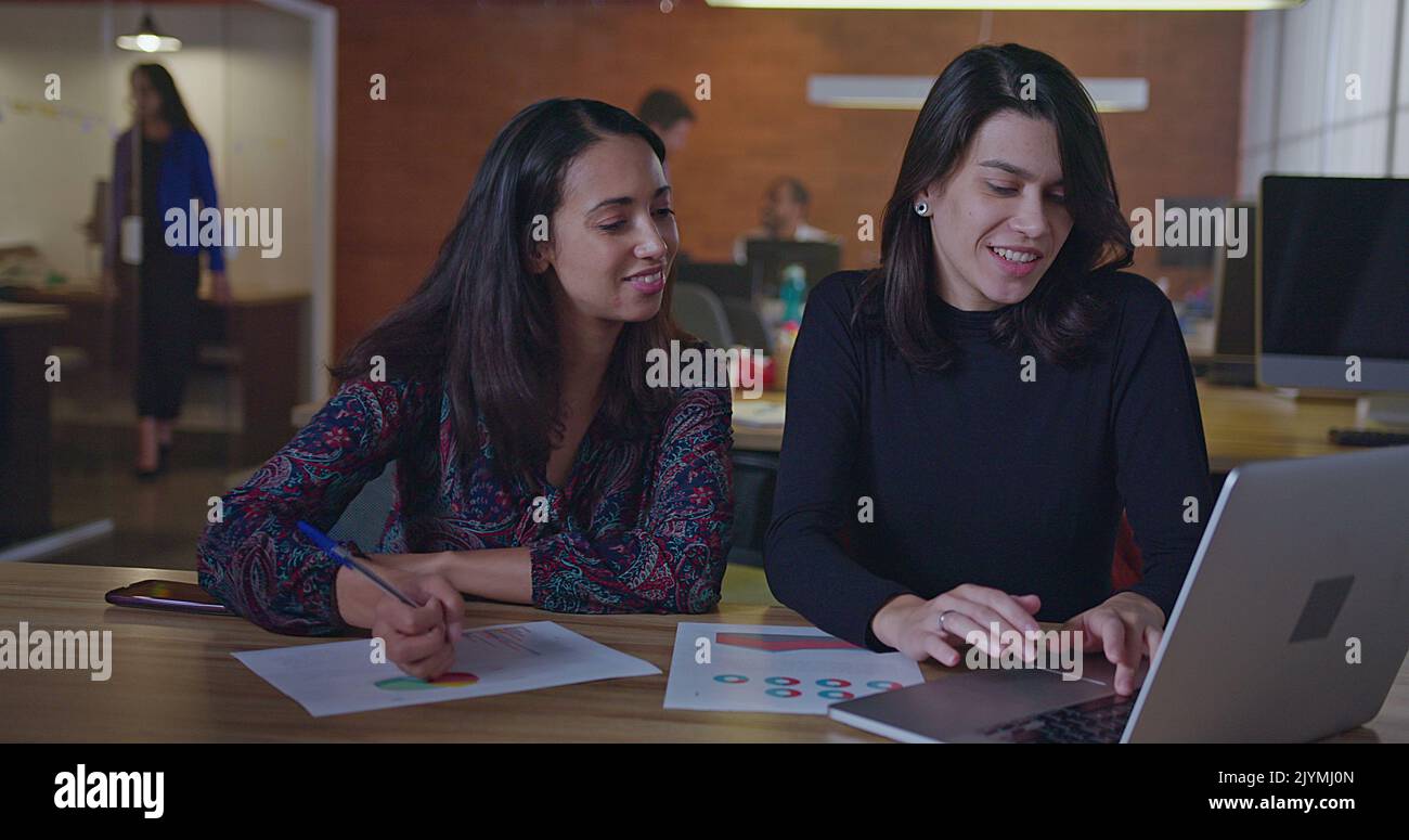 Two diverse female employees working at night in front of computer ...