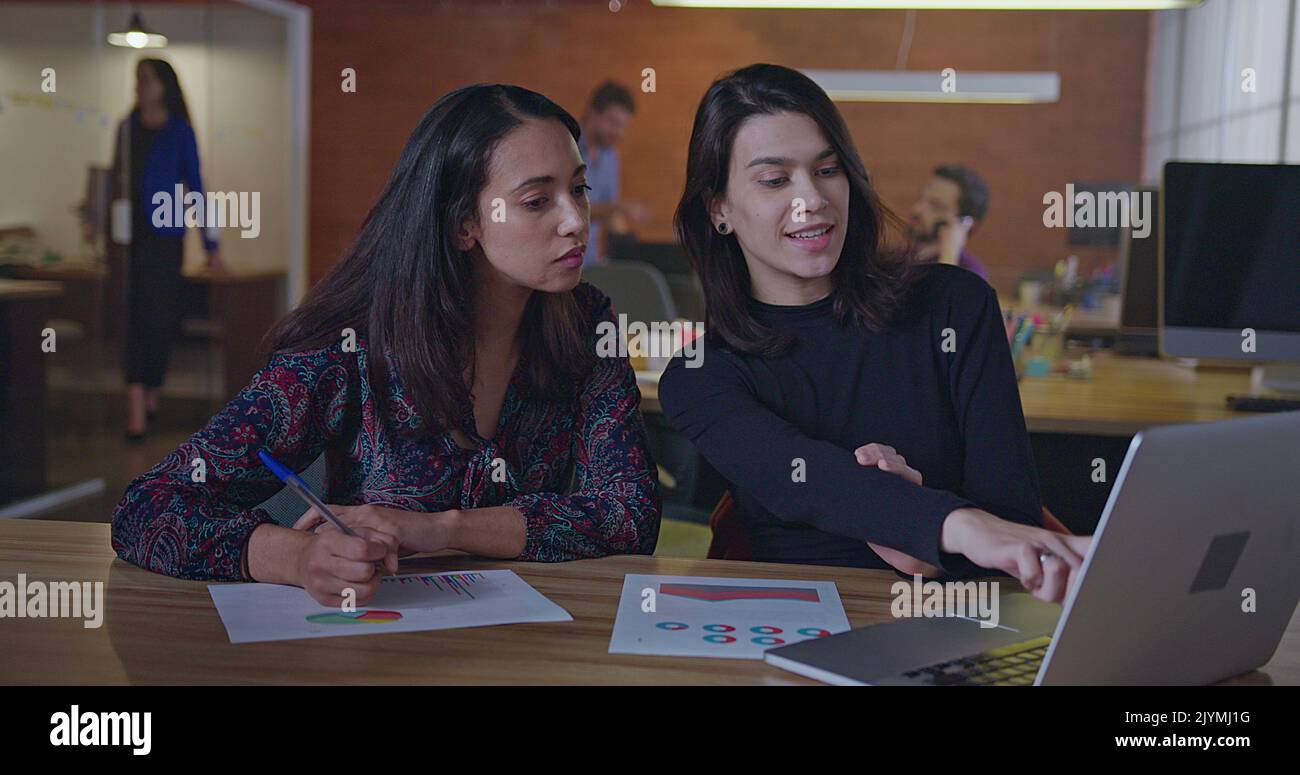Two diverse female employees working at night in front of computer ...
