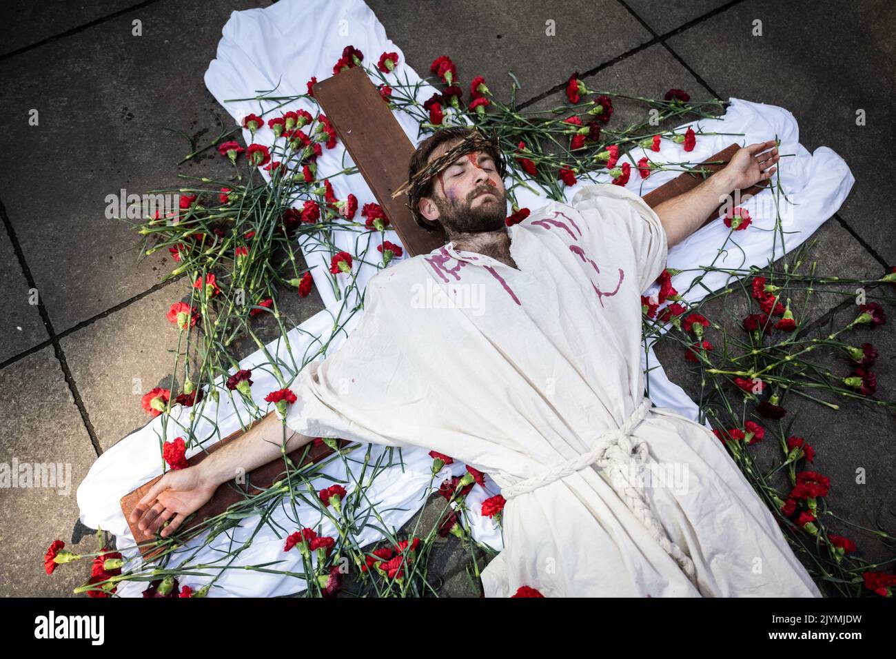 Tim Watkins portraying Jesus lies on a cross surrounded by carnation ...