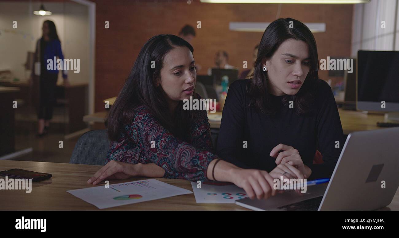 Two diverse female employees working at night in front of computer ...