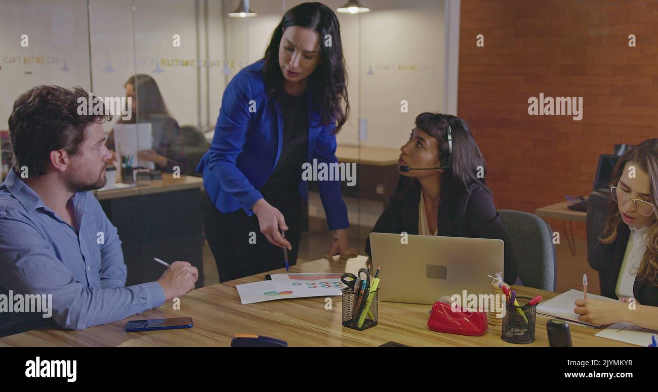 Female executive speaking with colleagues at corporate office at night ...