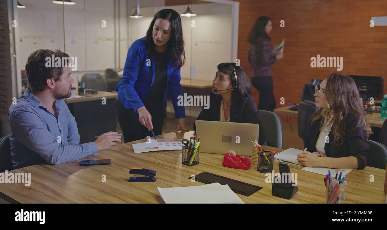 Female executive speaking with colleagues at corporate office at night ...