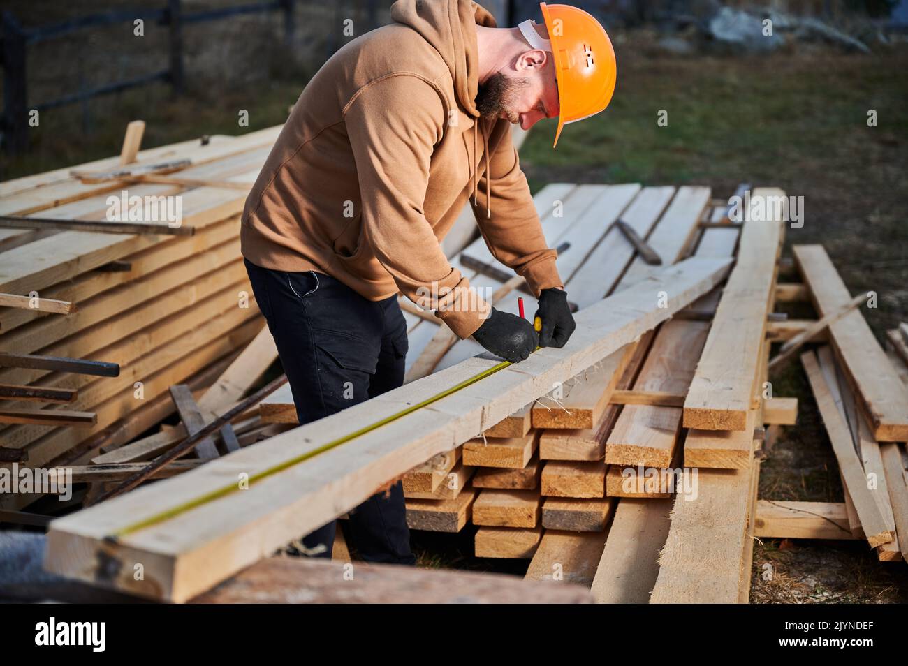 Man worker building wooden frame house. Carpenter using tape measure for measuring wooden planks ...