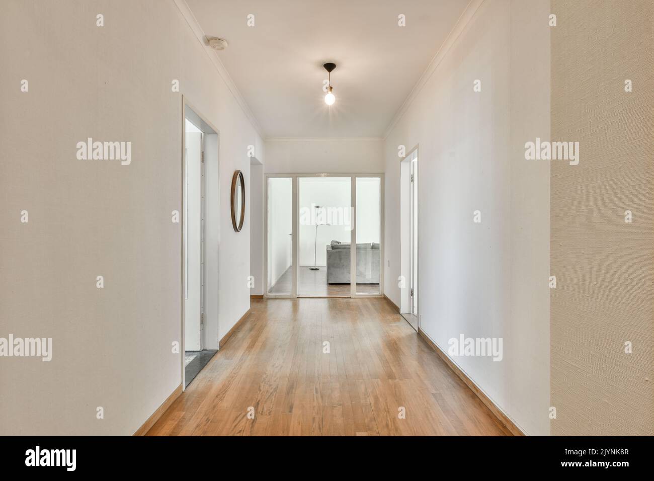Narrow corridor with white walls and doors leading to spacious room ...