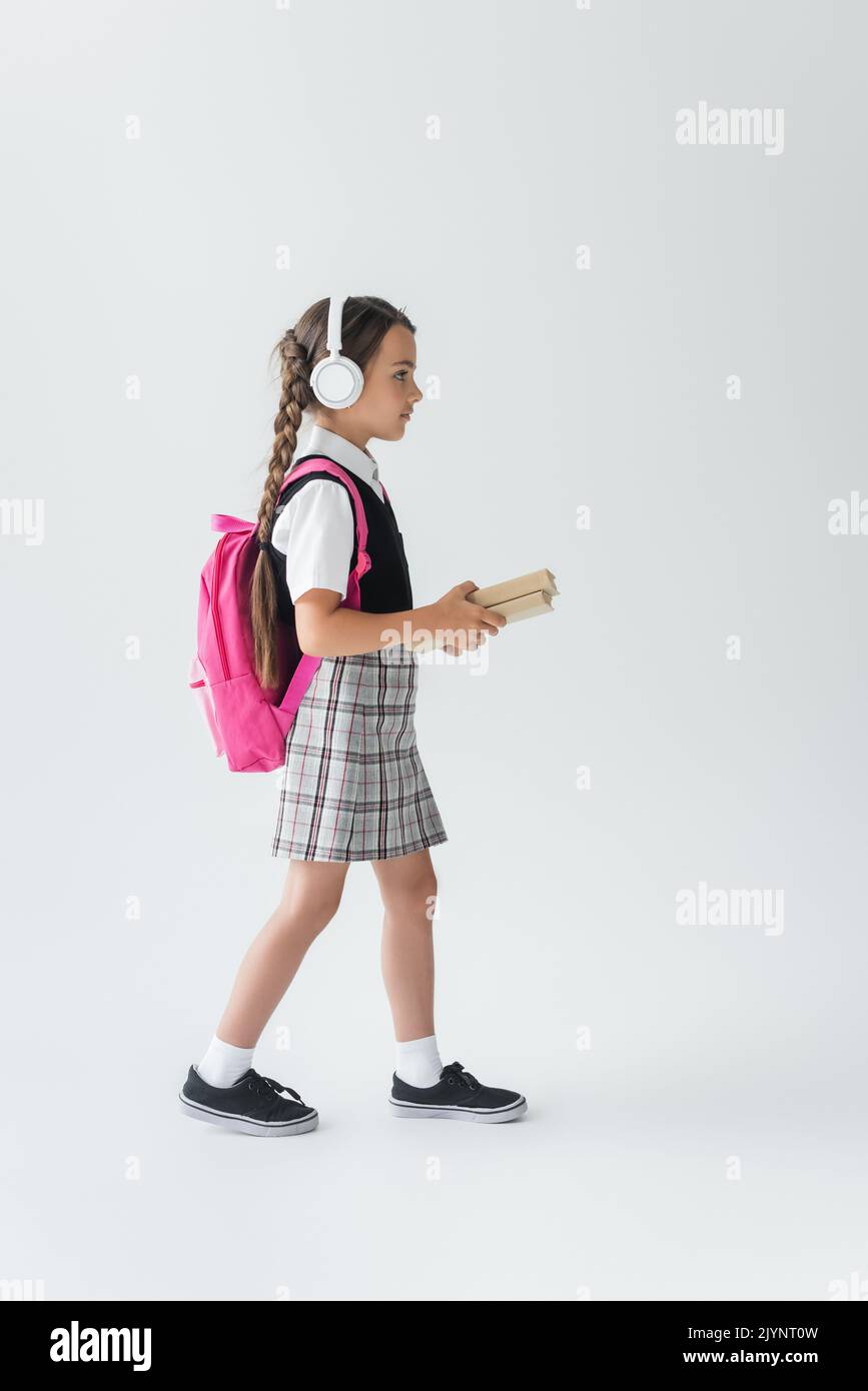 side view of girl in school uniform and wireless headphones walking ...