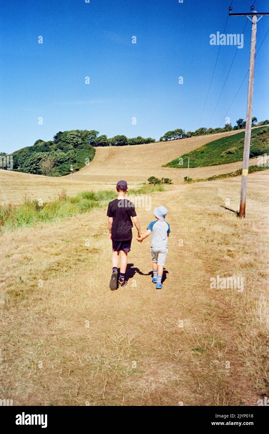 Brothers holing hands walking through a field, Hope Cove, Kingsbridge ...