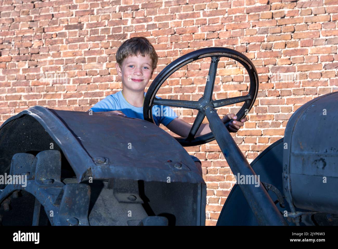 a boy driving an old vintage tractor in the background of a brick wall ...