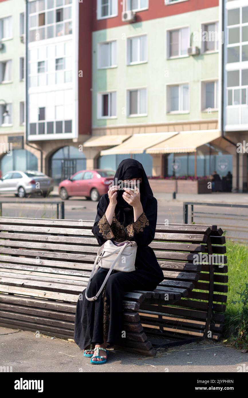 A Muslim woman is resting a bench in the park, tidying herself up by ...