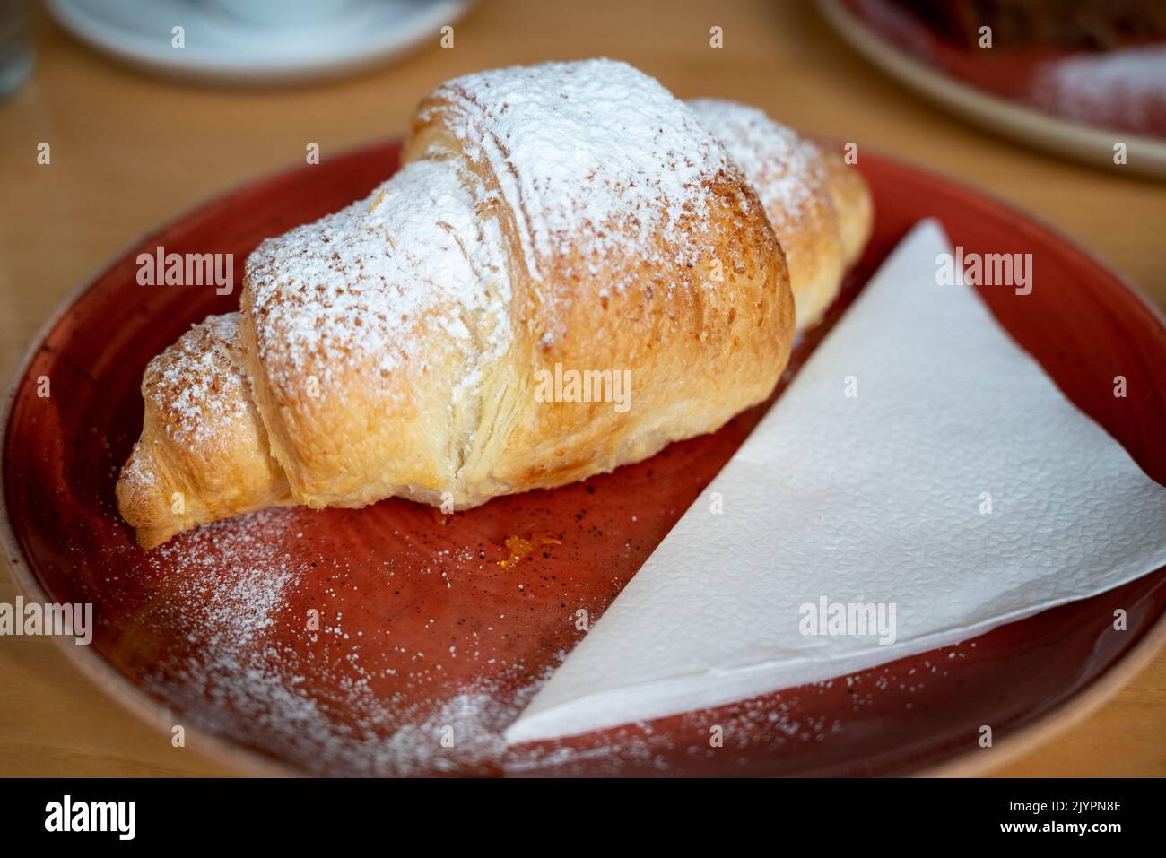 French butter croissant topped with powdered sugar, on a red plate next ...