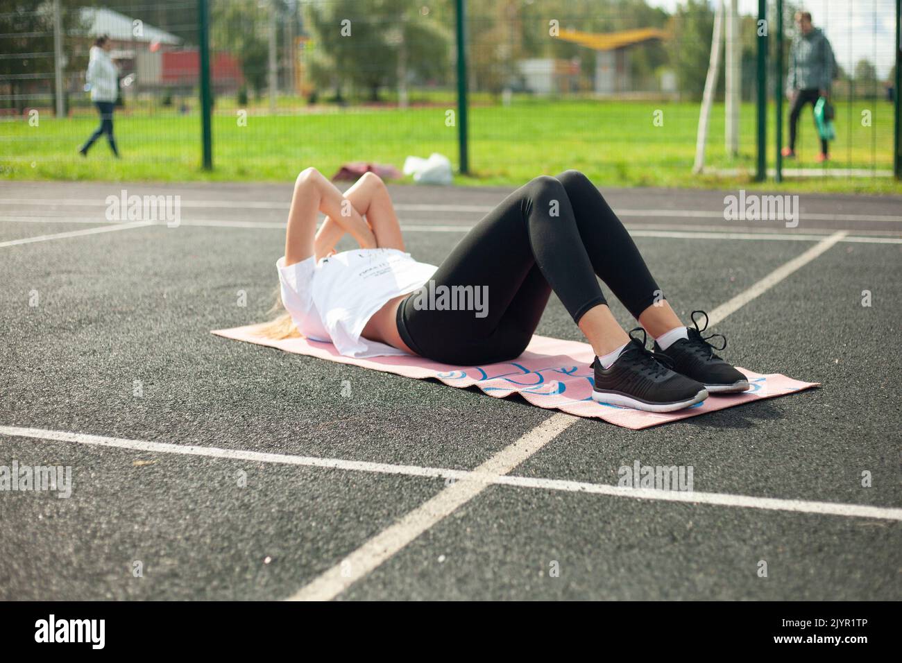 Girl pumps her abs in street. Fitness on sports ground. Young girl is ...