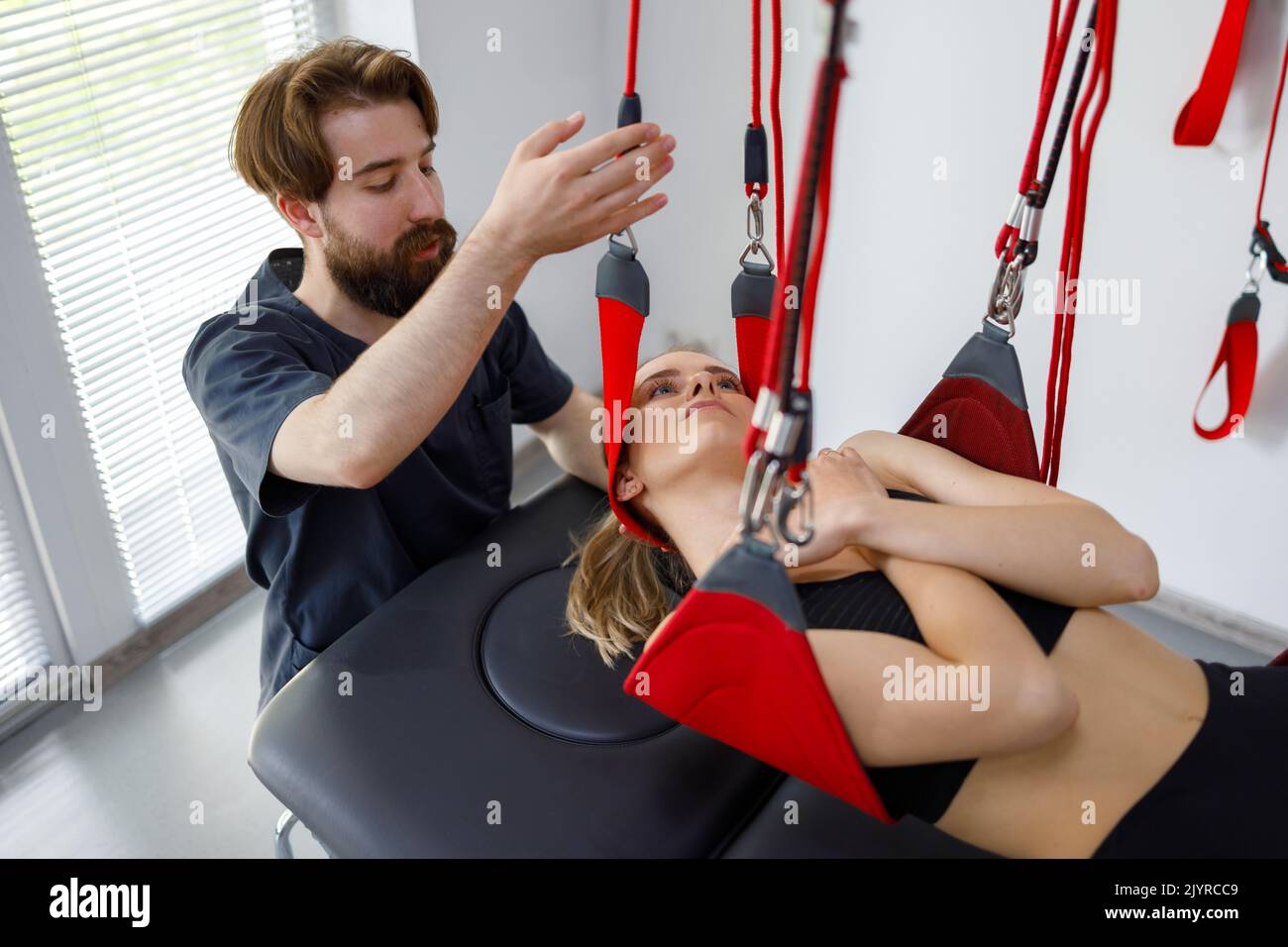 Physiotherapist assists female patient undergoing rehabilitative physiotherapy on a suspension ...