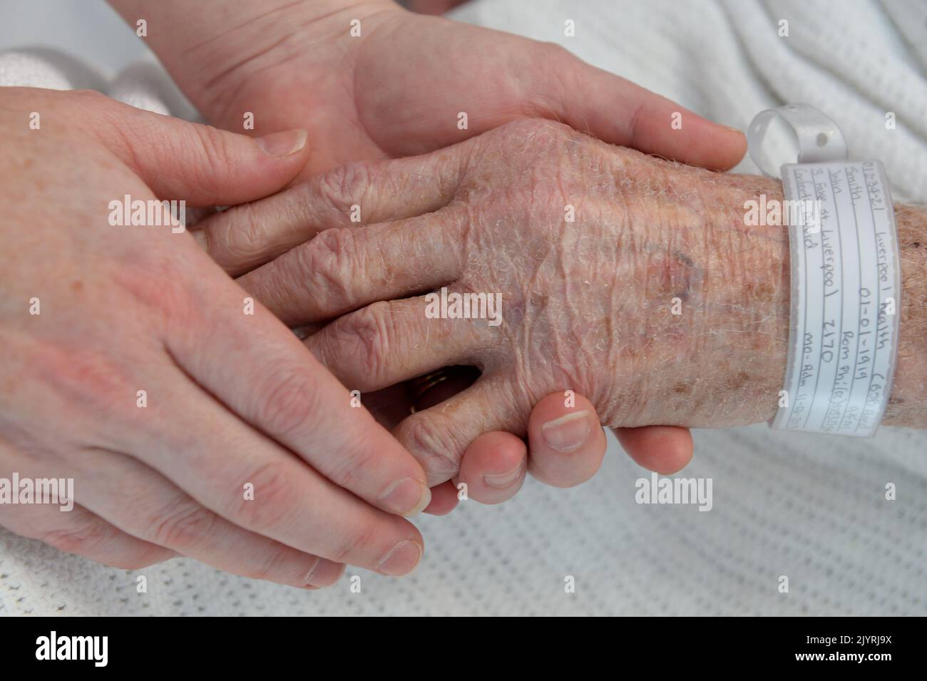 A nurse holds the hand of an elderly patient wearing a hospital ...