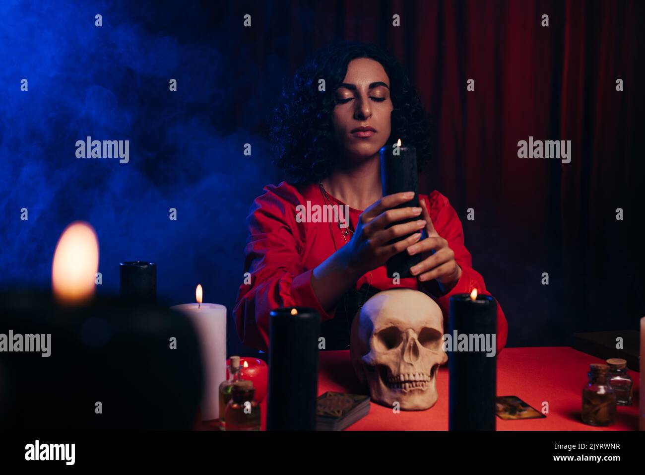 oracle with closed eyes holding burning candle near skull and blue ...