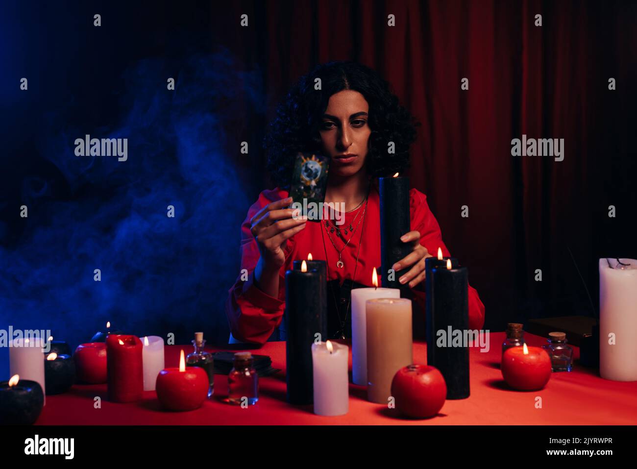 brunette fortune teller holding tarot card and burning candle on dark ...