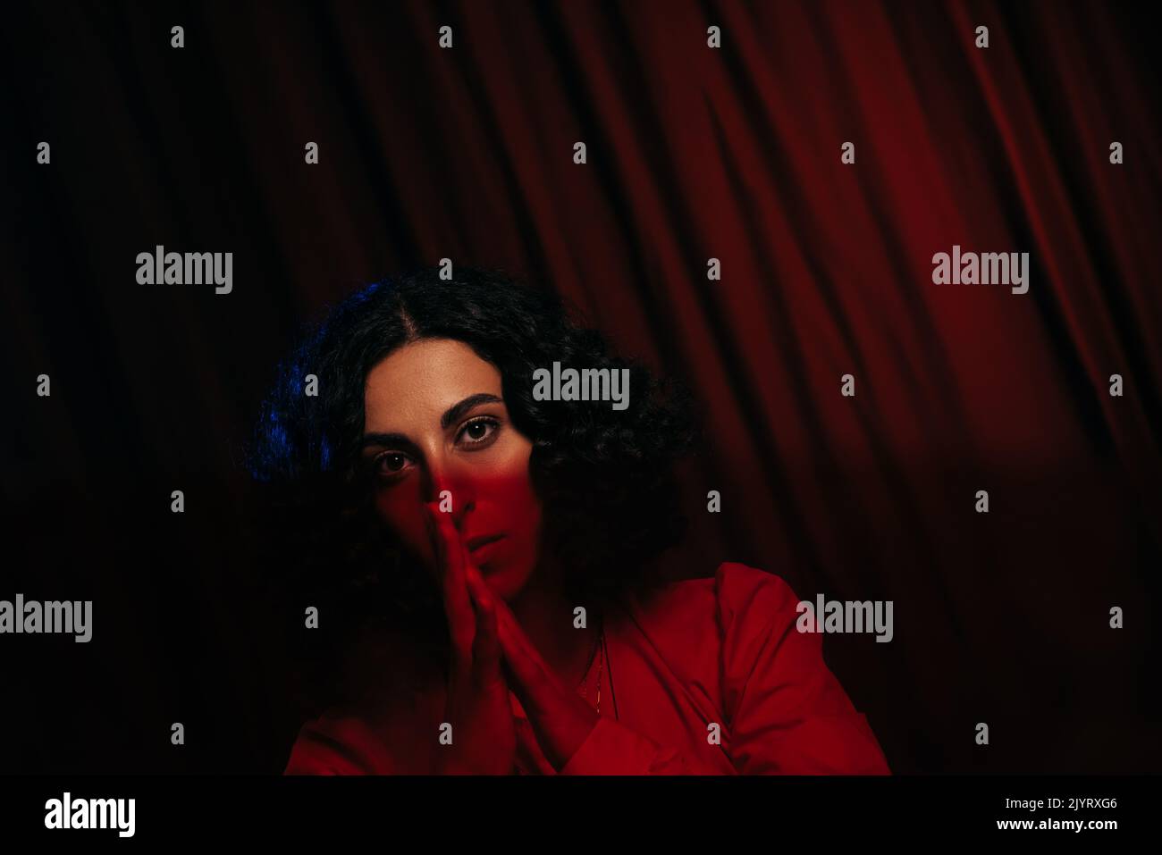 brunette oracle with folded hands near face looking at camera on dark ...