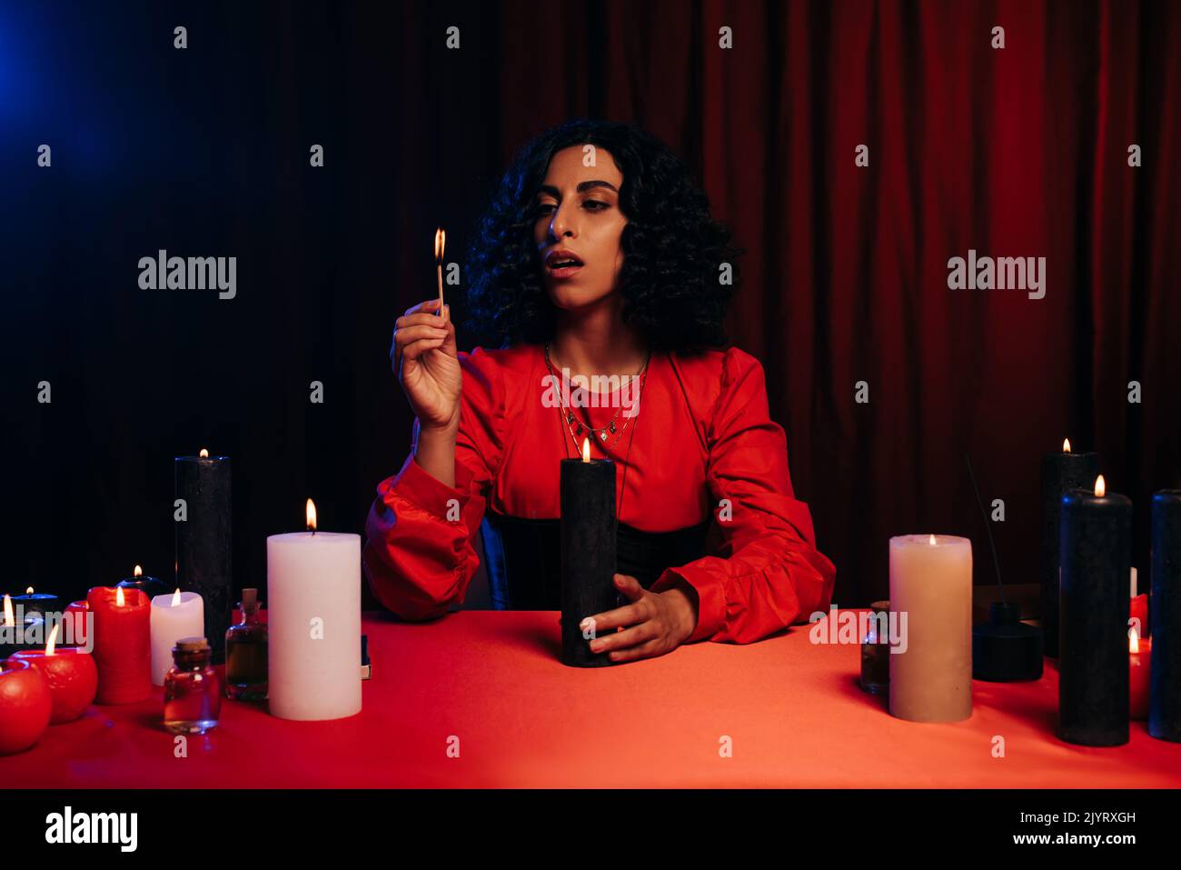 oracle with burning aroma stick near red table and candles in darkness ...