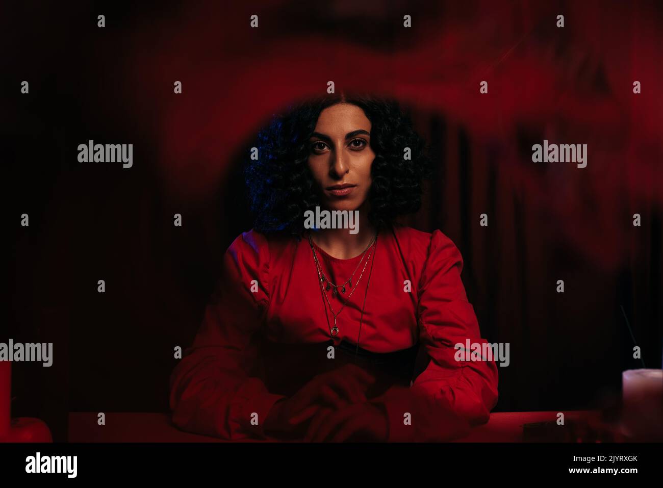 young fortune teller looking at camera on dark background with red ...