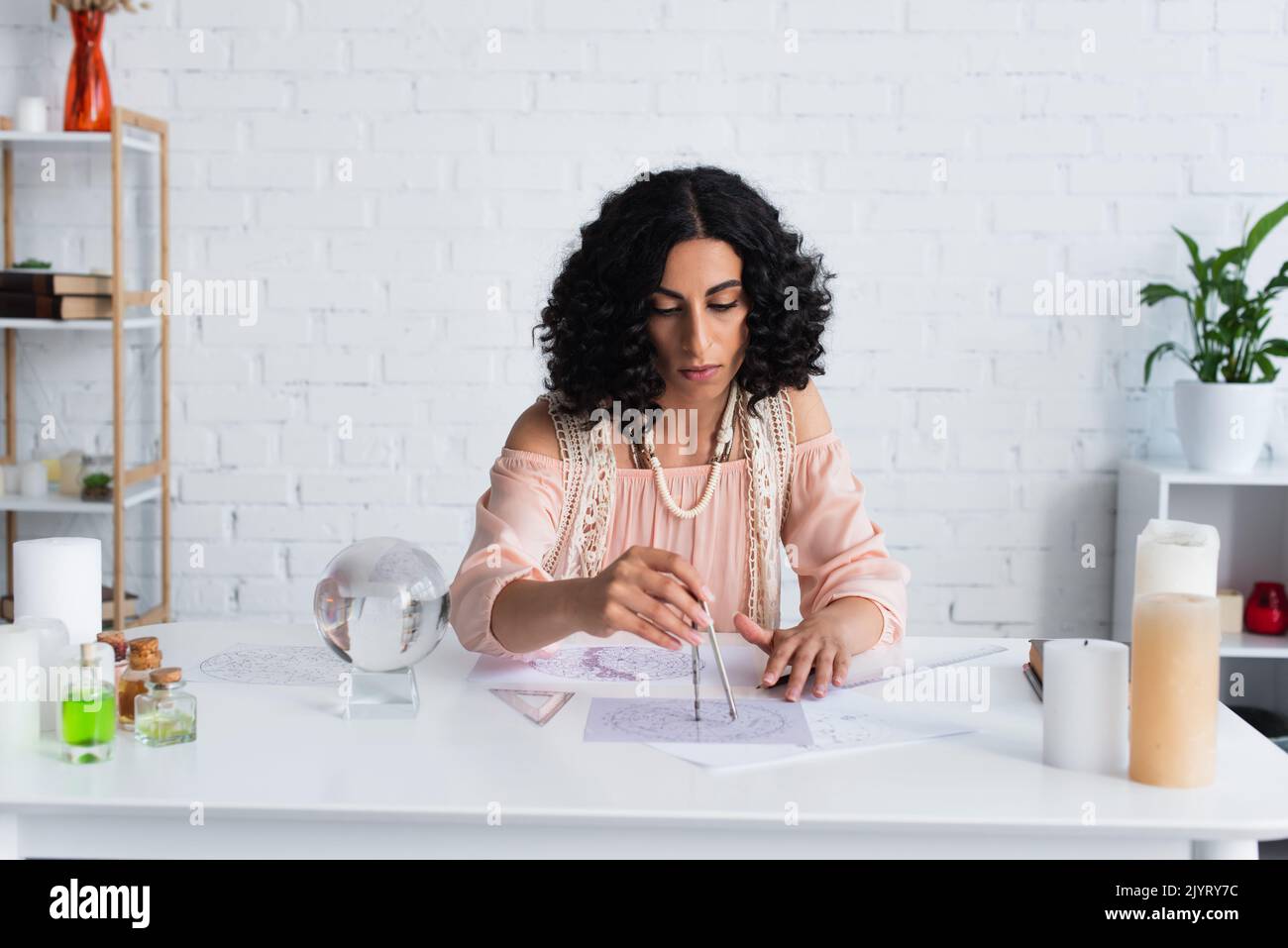 young astrologist drawing star charts near crystal ball and candles at ...