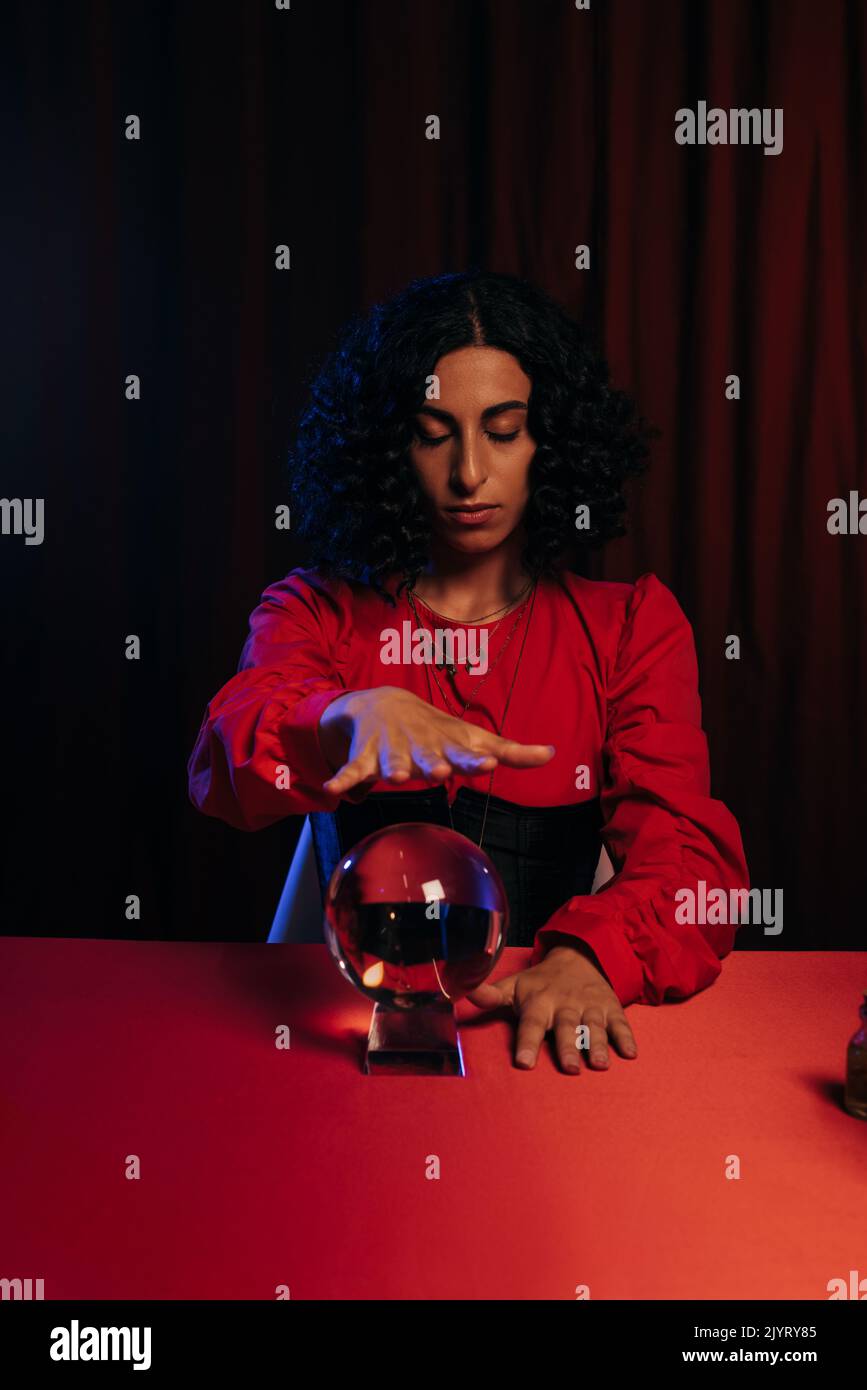 brunette fortune teller with closed eyes holding hand over crystal ball ...