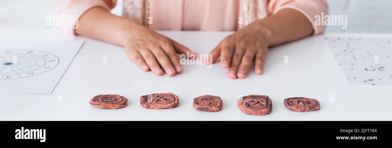 partial view of fortune teller sitting near clay runes and star charts ...